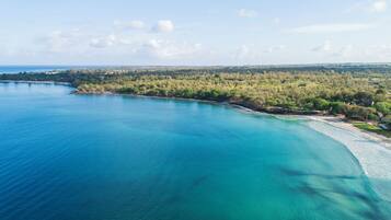Vista aérea de uma área costeira com águas turquesa cristalinas, uma praia arenosa e uma península densamente arborizada.