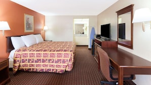 Quarto de hotel com cama, escrivaninha, cadeira, televisão e espelho.