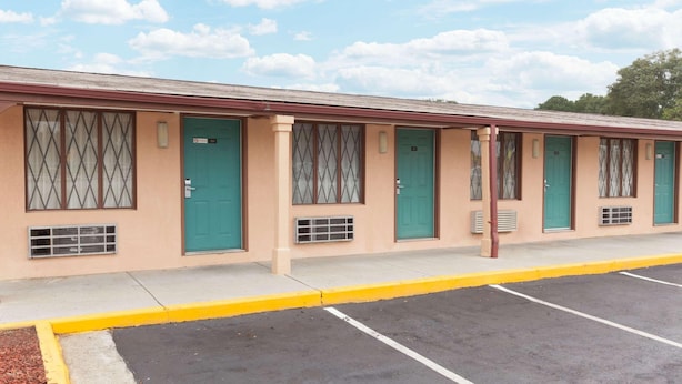 Um motel com uma fileira de quartos, cada um com porta verde e janela com padrão de losangos.