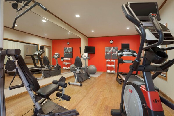 Uma academia com equipamentos de cardio, pesos e espelhos.
