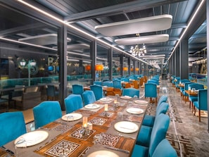 Um restaurante amplo com mesas grandes, cadeiras azuis e iluminação moderna.