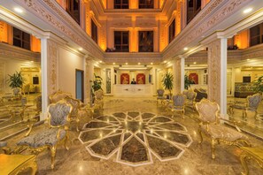 Um hall imponente com colunas ricamente decoradas, um design de carpete floral central e assentos luxuosos.