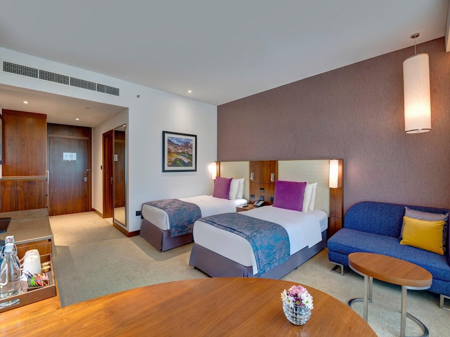 Quarto de hotel com duas camas, um sofá, uma mesa de centro e uma televisão.