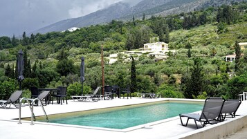 Área de piscina com espreguiçadeiras e vista para uma paisagem montanhosa.