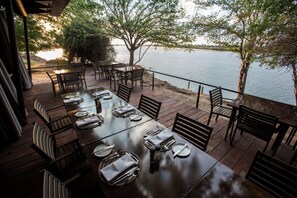 Um terraço com mesas preparadas para refeições, com vista para um corpo de água.