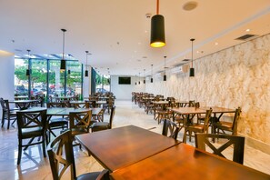 Um restaurante espaçoso com várias mesas e cadeiras, design moderno no teto e uma grande janela com vista para a rua.
