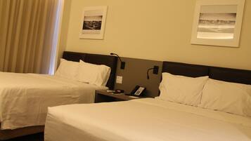 Quarto de hotel com duas camas, uma mesa de cabeceira com telefone e duas imagens emolduradas na parede.