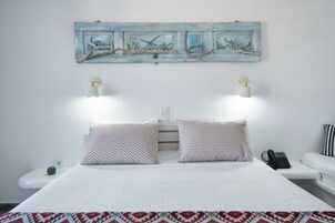 Uma cama bem arrumada com almofadas estampadas, uma obra de arte na parede, abajures e um telefone na mesinha de cabeceira.