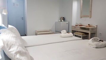 Quarto de hotel com duas camas, uma escrivaninha, uma kitchenette pequena e um espelho na parede.