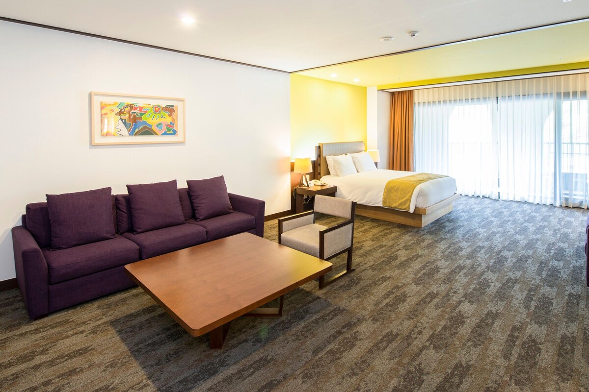 Quarto de hotel com sofá, cama, escrivaninha e um quadro na parede.