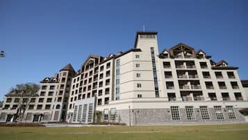 Um hotel com vários andares, uma torre central, varandas e um gramado bem cuidado.