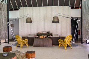 Uma área de recepção com um balcão, duas cadeiras amarelas, duas luminárias de chão e uma parede estampada.