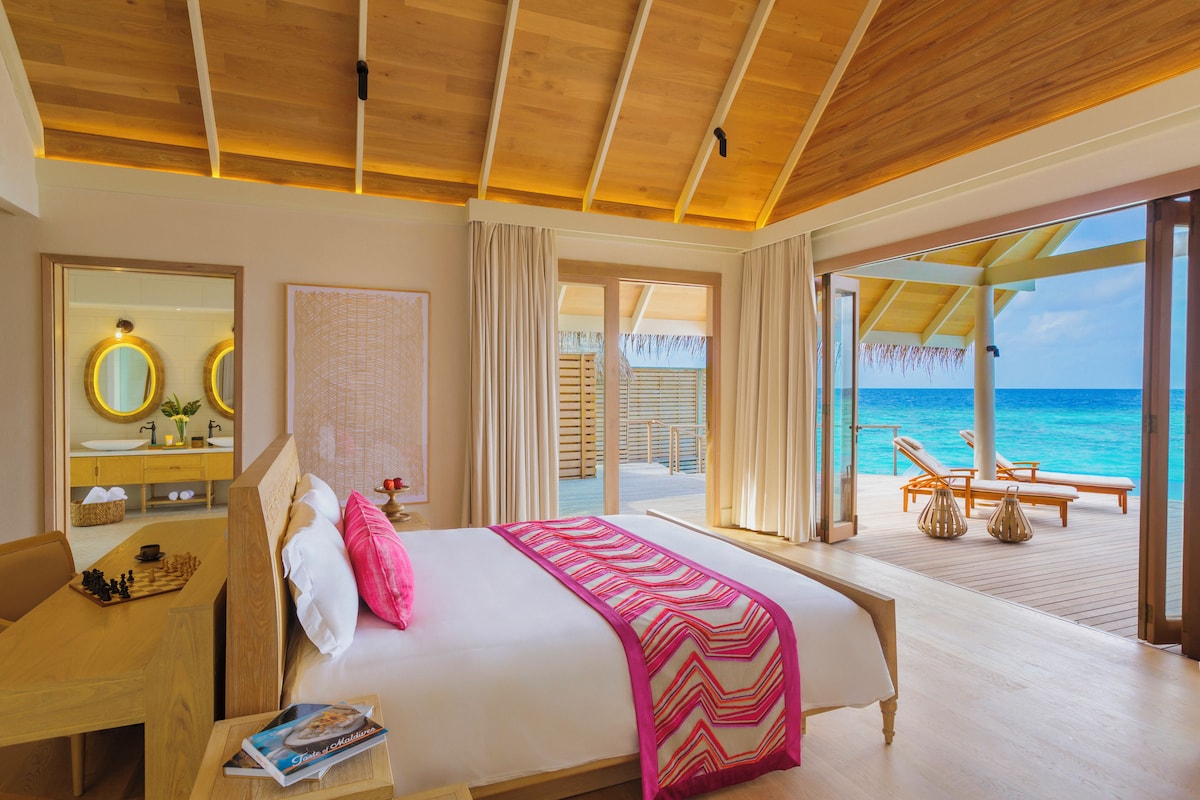 Quarto de hotel com uma cama, uma escrivaninha, um espelho e vista para o oceano.