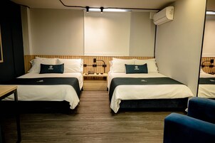 Quarto de hotel com duas camas, cada uma com cabeceira de madeira, mesa de cabeceira e abajur.