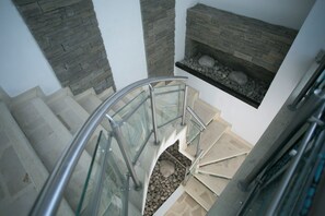 Escadaria em espiral com guarda-corpos de vidro que conduz a uma parede de pedra com lareira embutida.