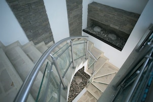 Escadaria em espiral com guarda-corpos de vidro que conduz a uma parede de pedra com lareira embutida.