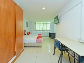 Quarto com cama, escrivaninha, cadeira, televisão e guarda-roupa.