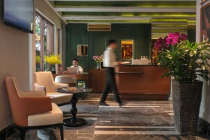 Um hall de hotel com balcão de recepção, área de estar e uma grande planta em vaso.