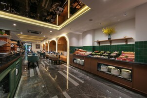 Um hall de hotel moderno, com piso de mármore, espaço para buffet com expositores de comida e área de estar com mesas e cadeiras.