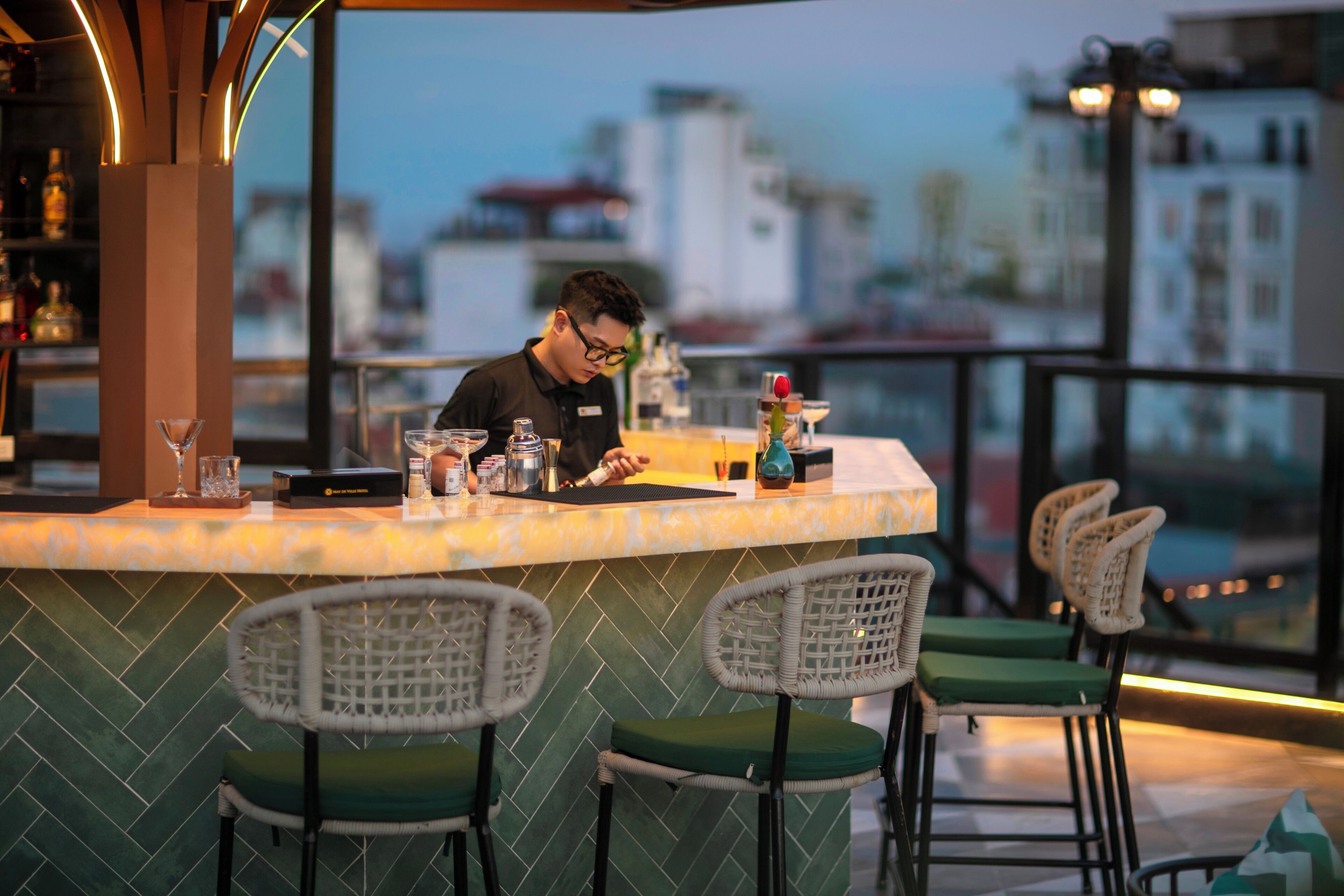 Uma área de bar com vista para a cidade, banquetas e um bartender.