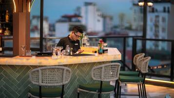 Uma área de bar com vista para a cidade, banquetas e um bartender.
