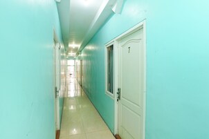 Um corredor com paredes verde-água e portas brancas, que leva a um quarto claro no final.