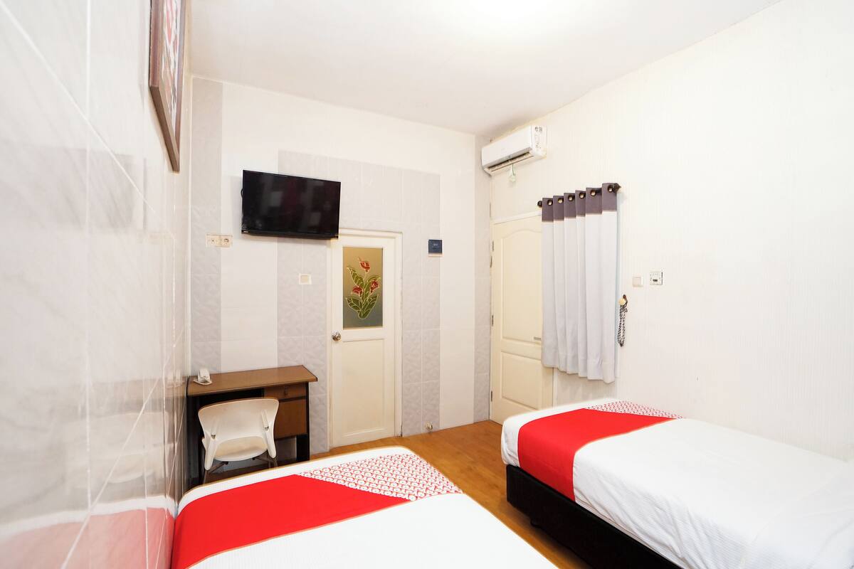 Quarto de hotel com duas camas, televisão, escrivaninha e porta com pintura floral.