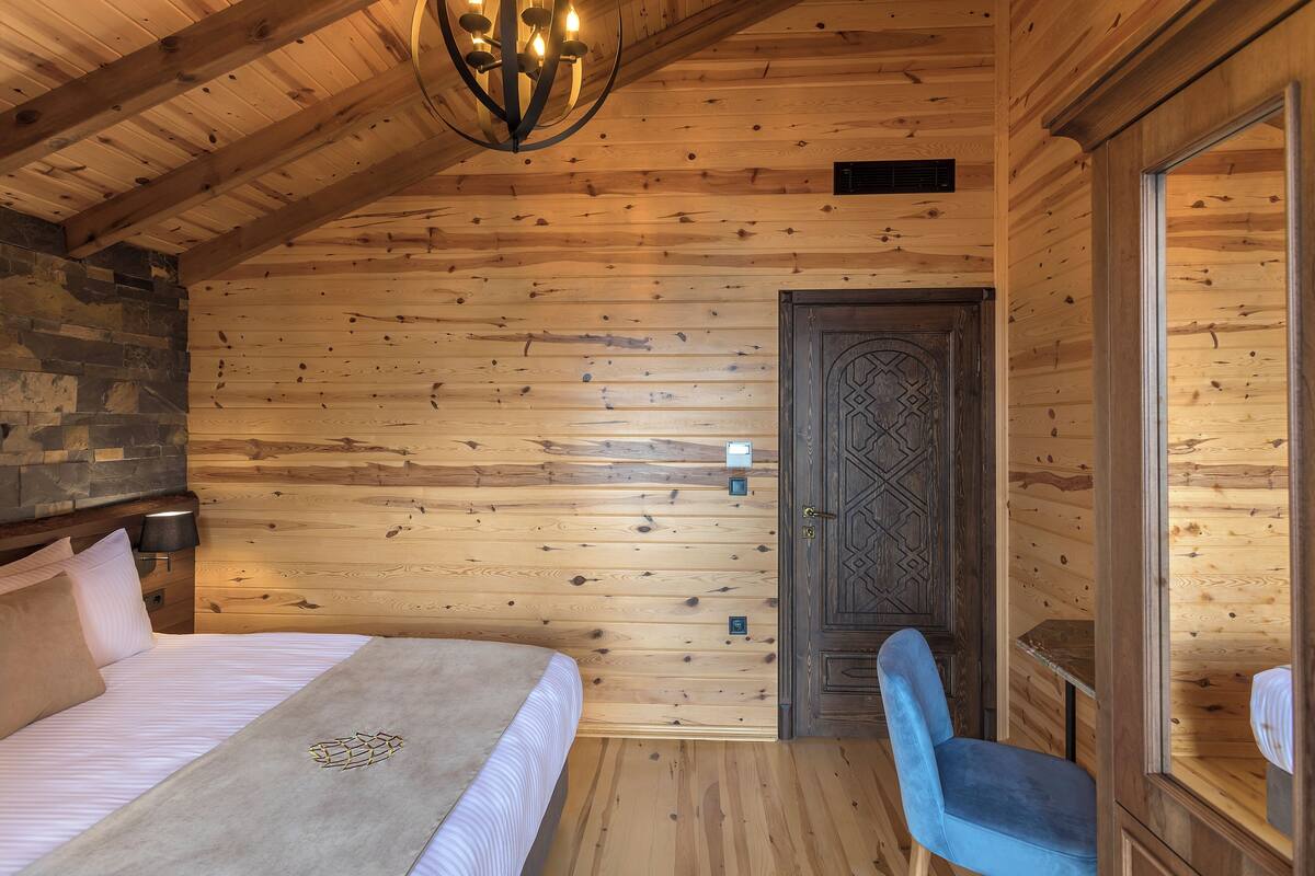 Um quarto de cabana de madeira com uma cama, uma cadeira, uma parede de pedra e uma porta de madeira.
