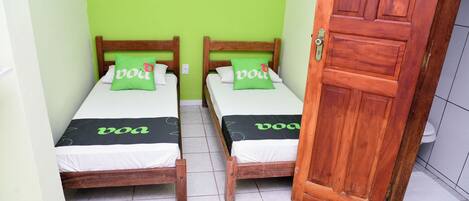 Quarto com duas camas de madeira, cada uma com travesseiro verde e colchão branco, e uma porta de madeira.
