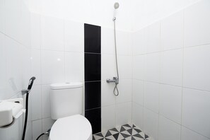 Casa de banho com azulejos brancos, um detalhe vertical preto, uma sanita e um chuveiro com manguera.