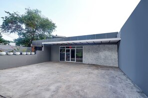 Um edifício moderno com telhado plano, entrada por porta de vidro e pátio de concreto.