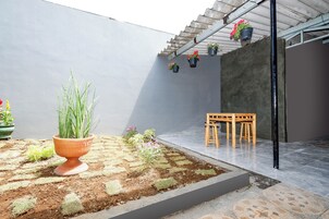 Um pátio com planta em vaso, um banco de madeira e vasos de flores pendurados.
