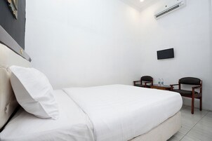 Quarto de hotel com cama, televisão na parede e duas cadeiras.