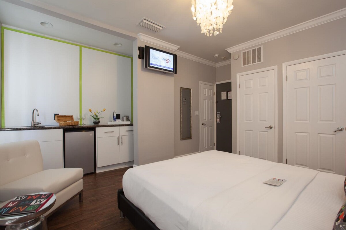 Quarto de hotel com cama, escrivaninha, cadeira, televisão e armário.