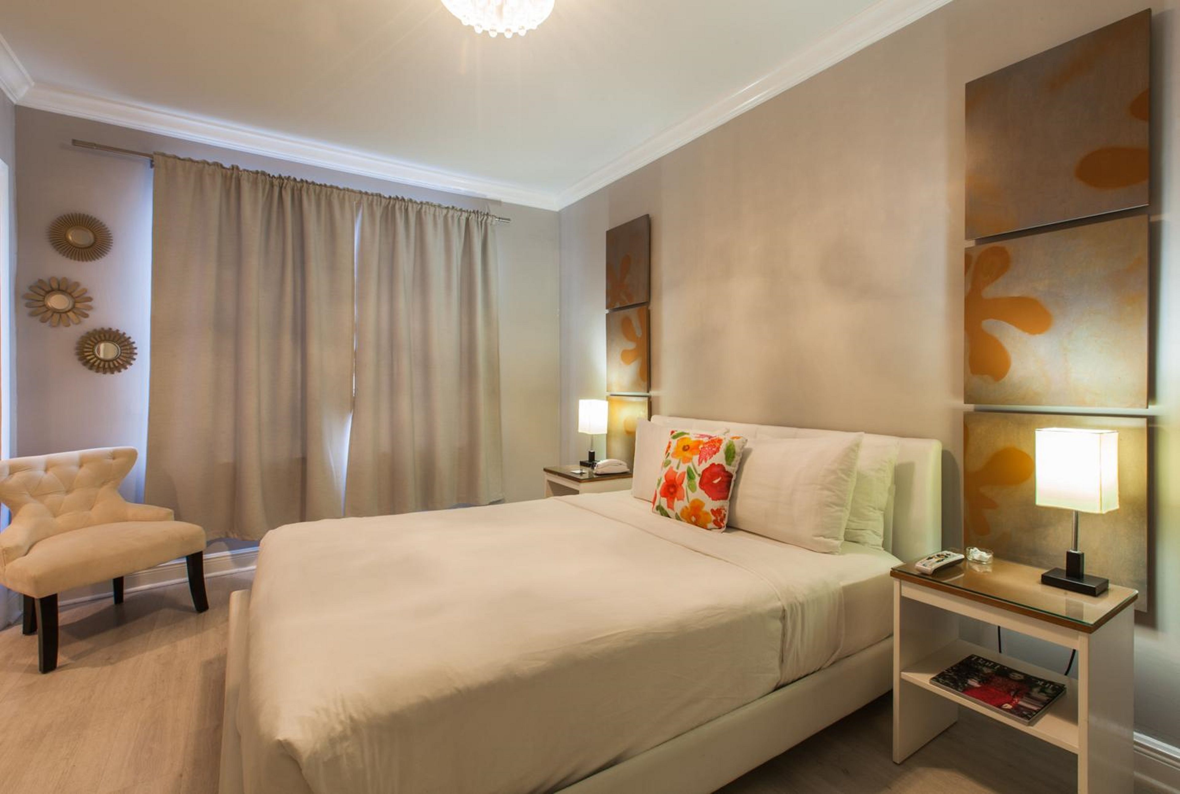 Quarto de hotel com uma cama grande, uma cadeira, mesas de cabeceira com luminárias e obras de arte nas paredes.