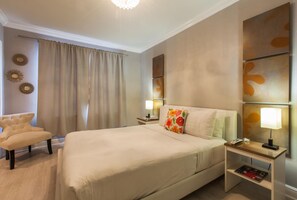 Quarto de hotel com uma cama grande, uma cadeira, mesas de cabeceira com luminárias e obras de arte nas paredes.