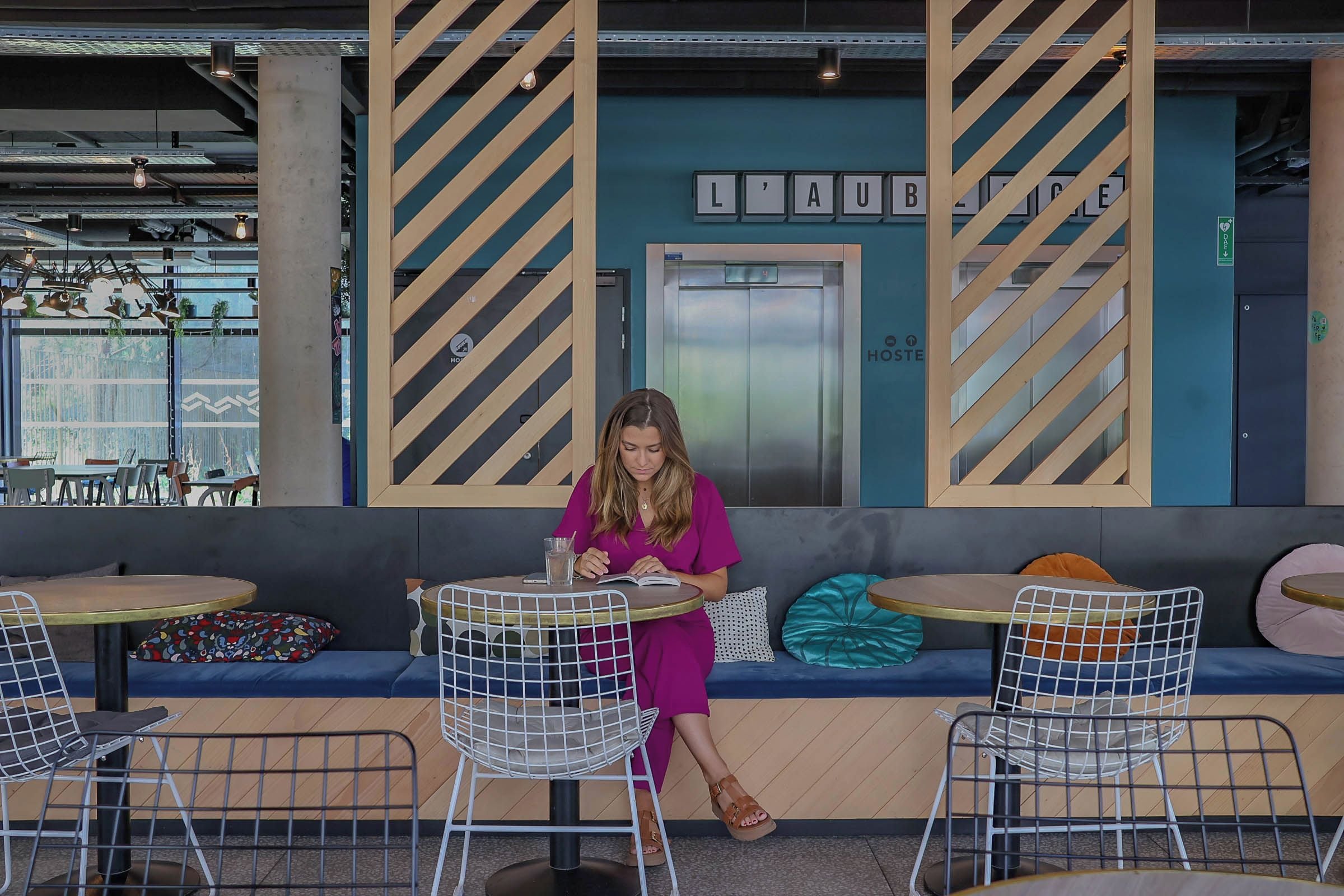 Mulher lendo à mesa em café moderno com parede azul e painéis listrados.