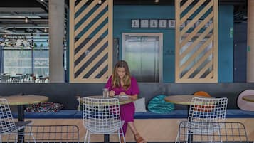 Mulher lendo à mesa em café moderno com parede azul e painéis listrados.