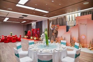 Salão de banquetes com mesas redondas, cadeiras vermelhas e palco decorado em vermelho.