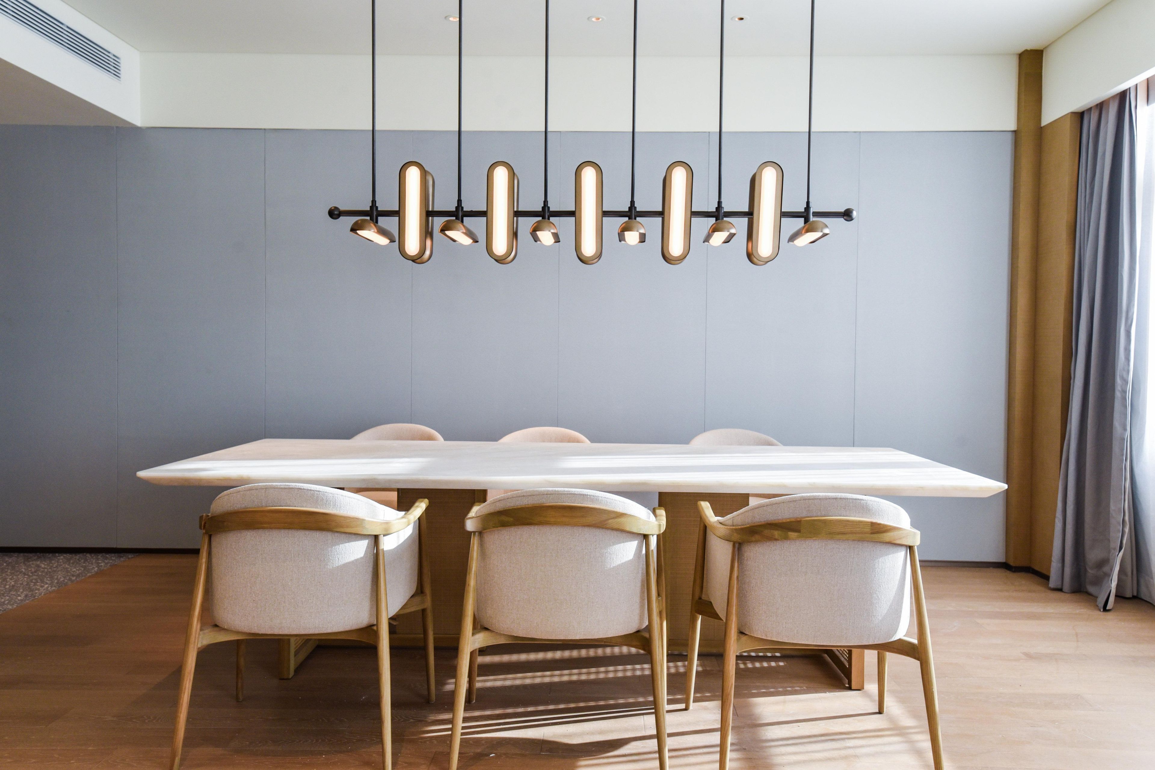 Uma sala de jantar moderna com uma mesa comprida, quatro cadeiras e uma luminária pendente singular.