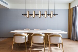 Uma sala de jantar moderna com uma mesa comprida, quatro cadeiras e uma luminária pendente singular.