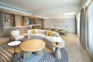 Quarto de hotel moderno com sofá, duas mesas redondas, área de jantar e estantes embutidas.