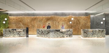 Uma área de recepção moderna com três balcões de mármore, parede com padrão de bambu e guarda-corpo de vidro.