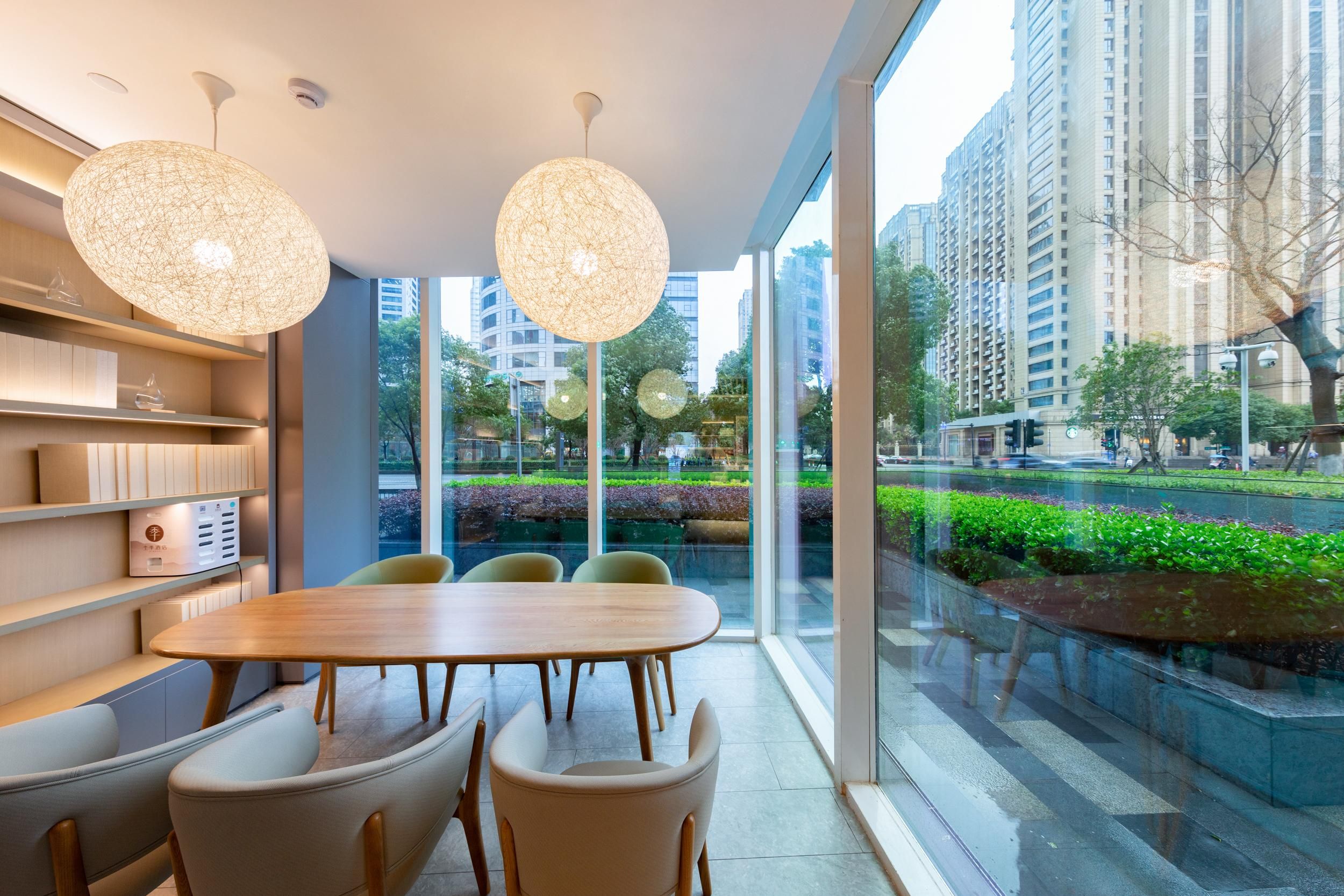 Uma área de jantar moderna com uma mesa e cadeiras de madeira, um lustre pendente grande e vista para um horizonte urbano através de amplas janelas.