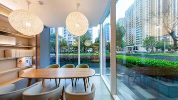 Uma área de jantar moderna com uma mesa e cadeiras de madeira, um lustre pendente grande e vista para um horizonte urbano através de amplas janelas.