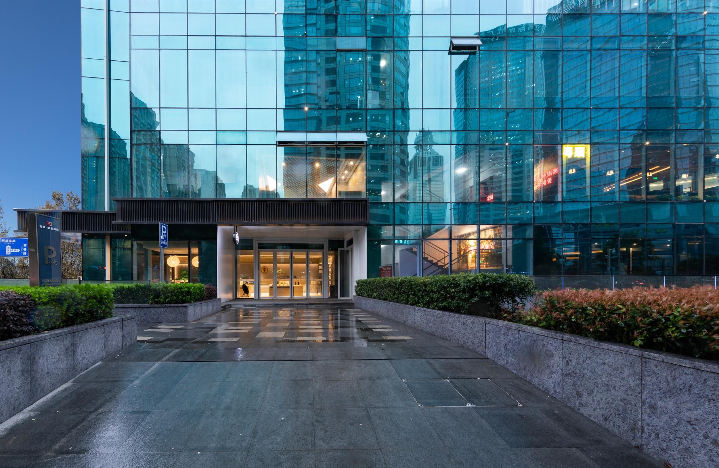 Um edifício moderno com janelas de vidro refletivas, entrada central e calçada pavimentada.