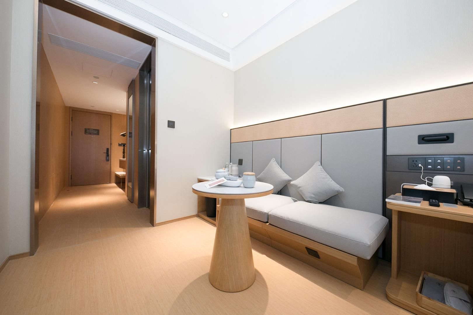 Quarto de hotel moderno com sofá, mesa redonda e escrivaninha com computador e telefone.
