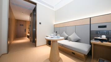 Quarto de hotel moderno com sofá, mesa redonda e escrivaninha com computador e telefone.