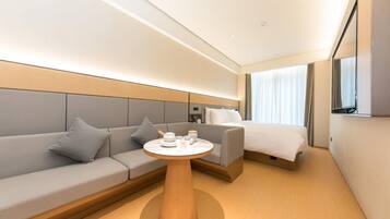 Quarto de hotel moderno com sofá, mesa de cabeceira, cama e televisão.