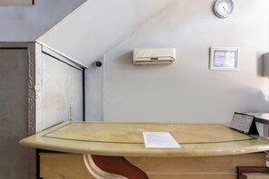 Quarto com escrivaninha, ar condicionado, relógio e um certificado emoldurado na parede.
